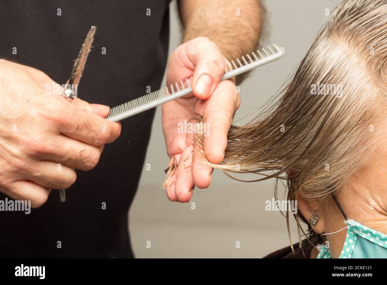 Professional hairdresser cutting a woman's hair with scissors and a ...