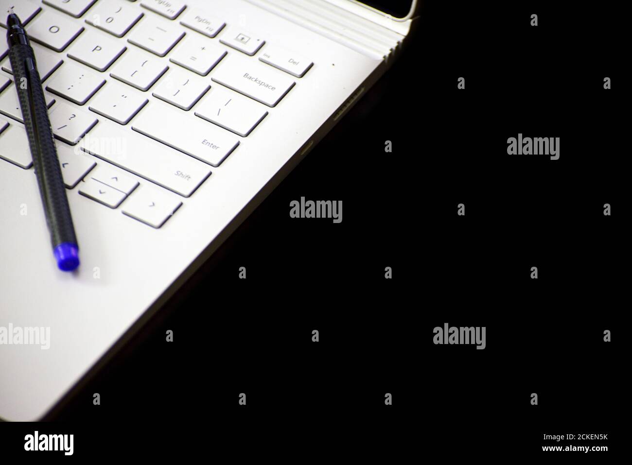 close-up of a pen lying down on laptop keypad against black background ...