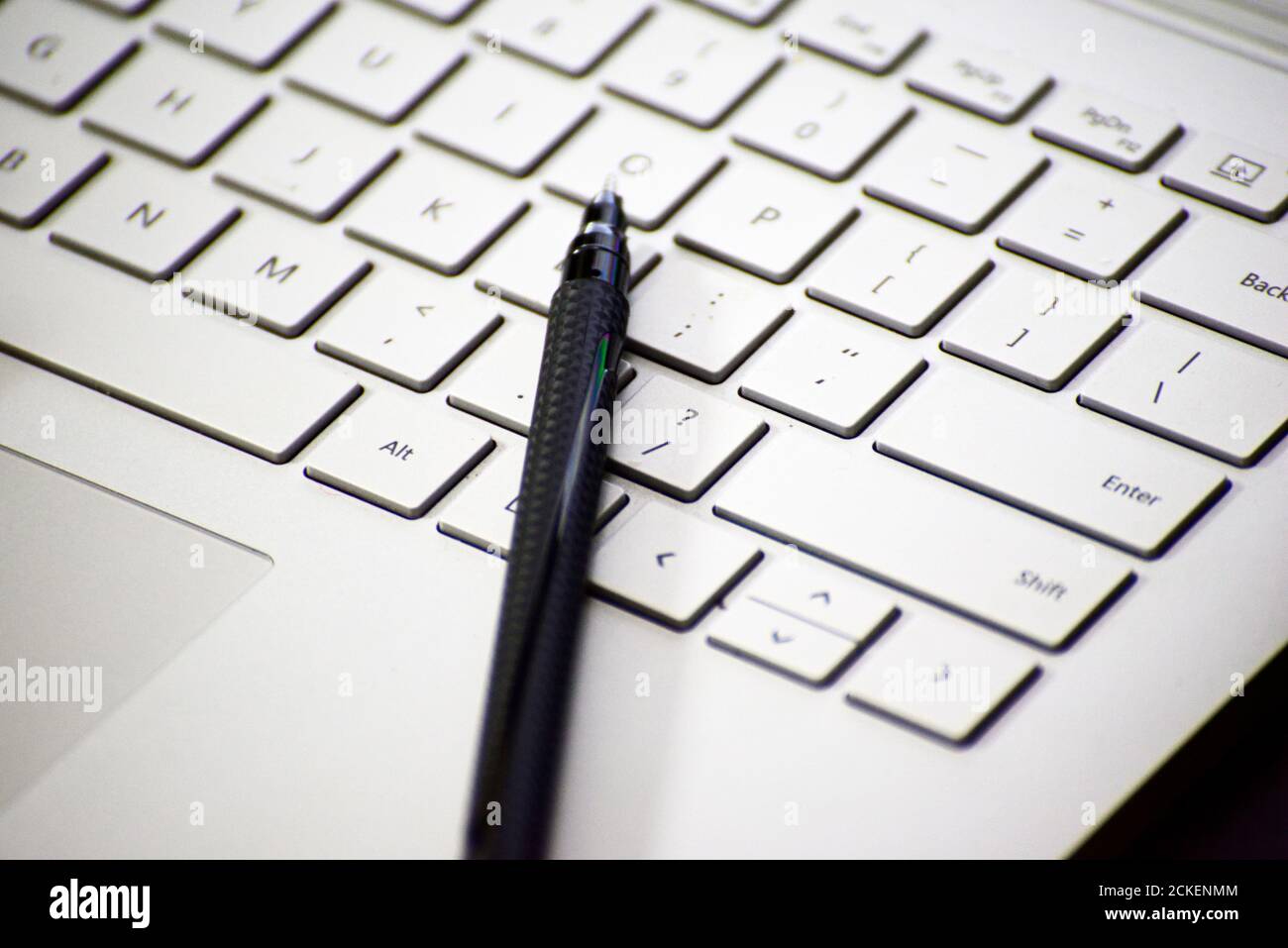 close-up of a pen lying down on laptop keypad against black background ...