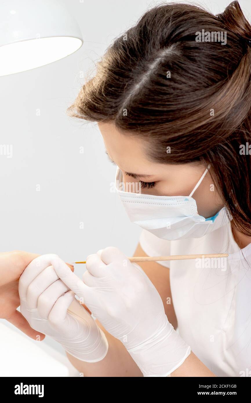 Manicure master with protective mask in rubber gloves applying beige ...