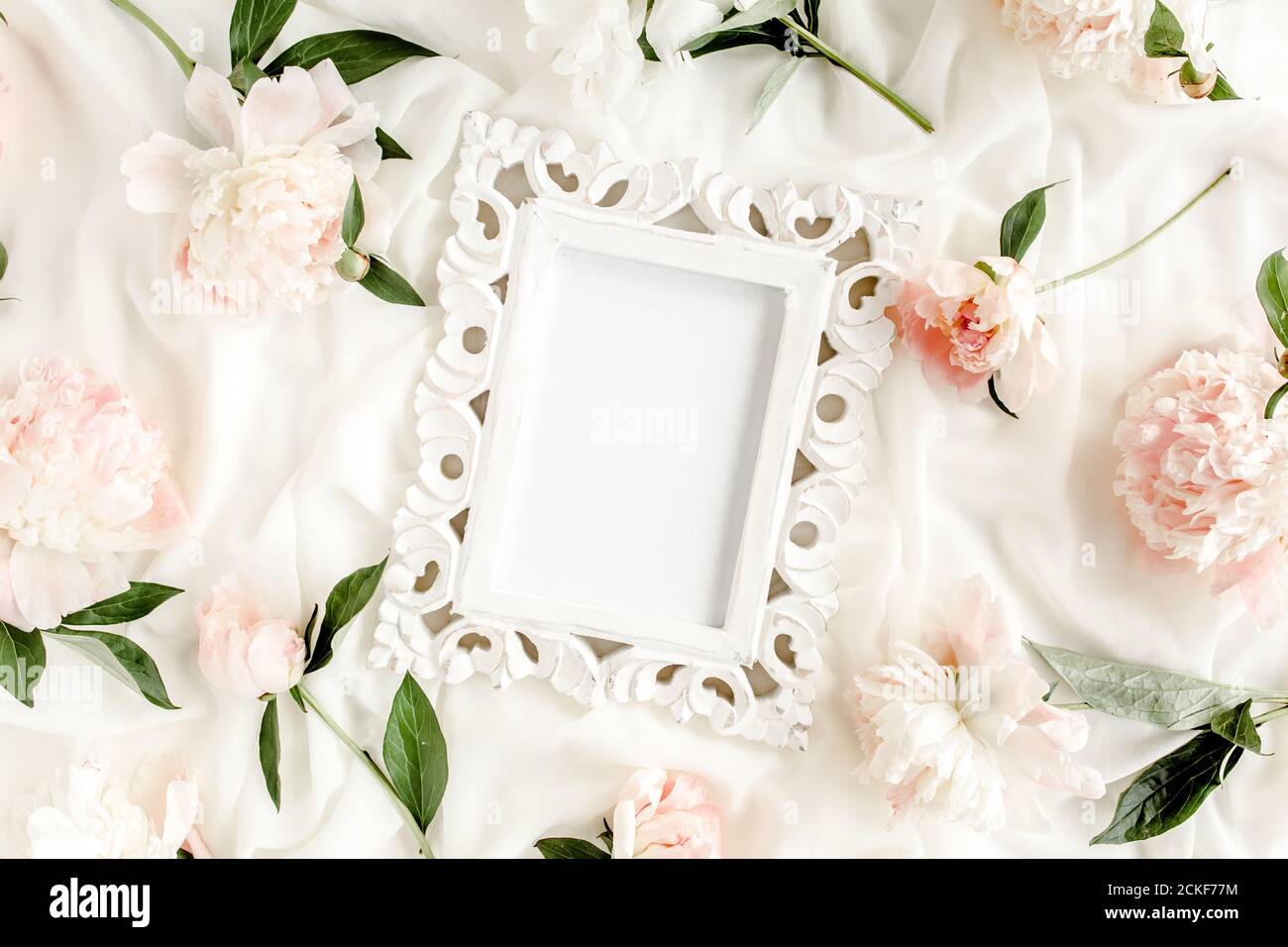 Carved, white frame decorated of beautiful and beige peonies. Flat lay ...