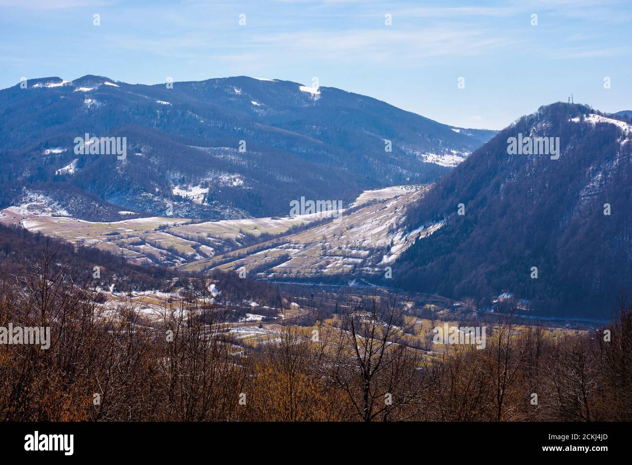 mountainous countryside in early spring. dry grass and leafless trees on the hillside. snow in ...
