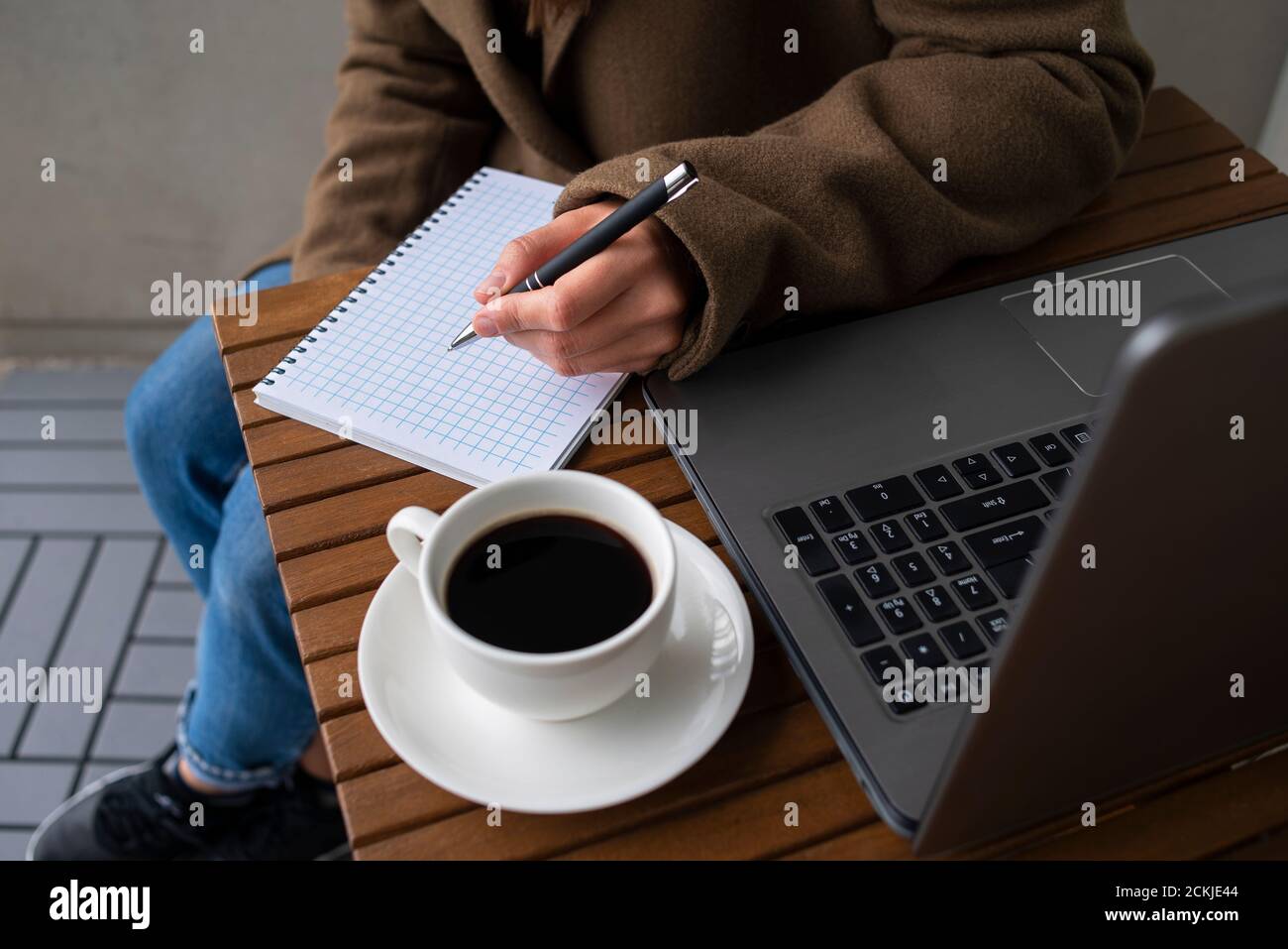 Woman in wool coat working in street cafe with laptop. Cup of coffee on ...
