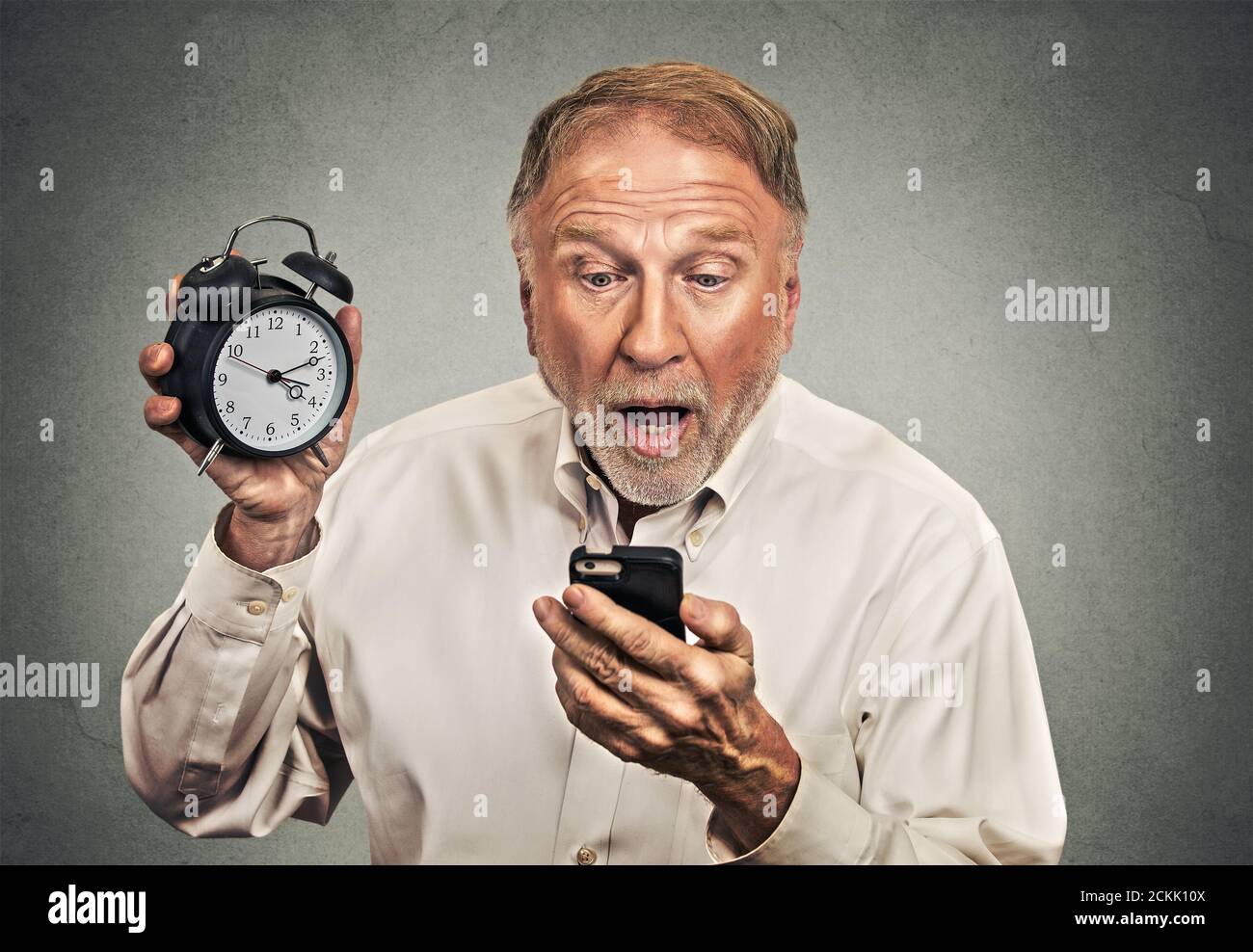 Portrait surprised business man with alarm clock looking at smart phone ...
