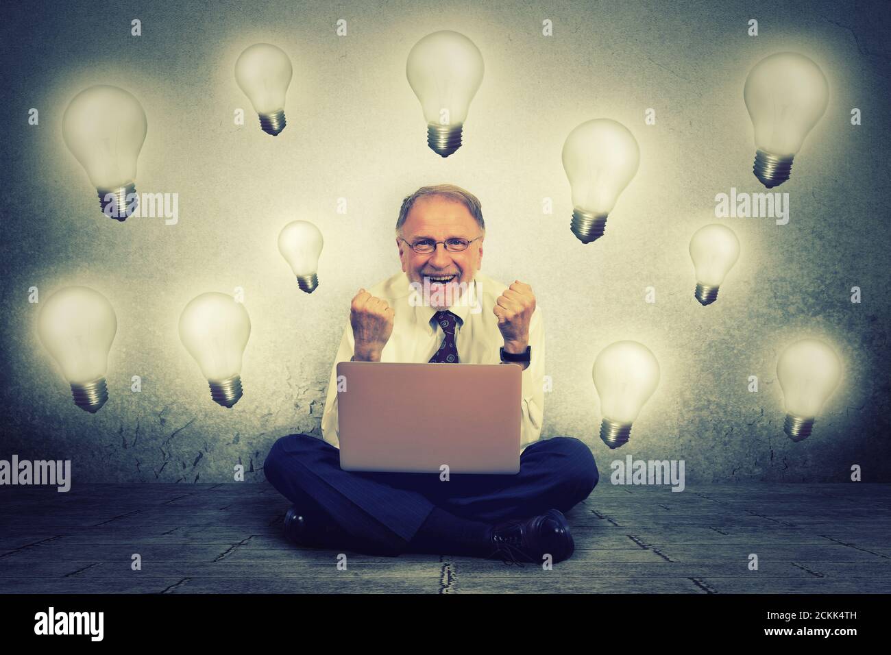 Senior man working on computer with light bulb plugged in it celebrates ...