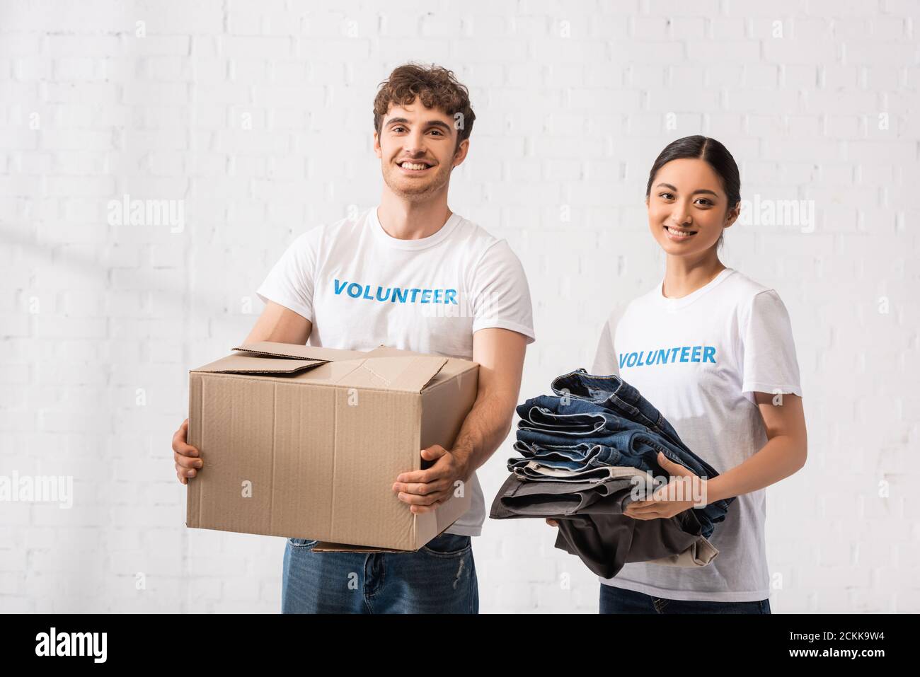 Multicultural volunteers holding package and clothes in charity center ...