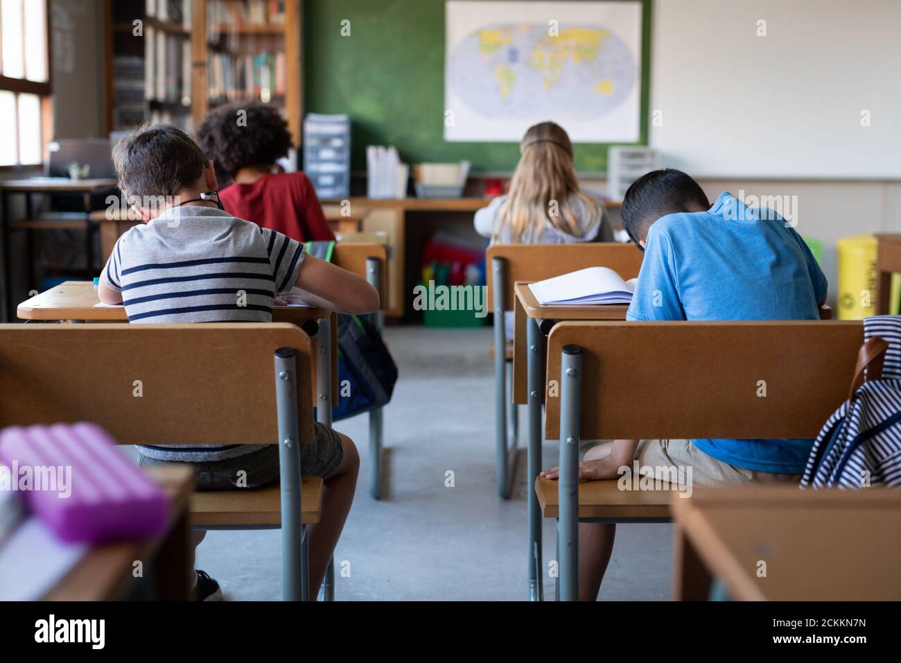 Rear view of group of kids studying while sitting on their desk at ...