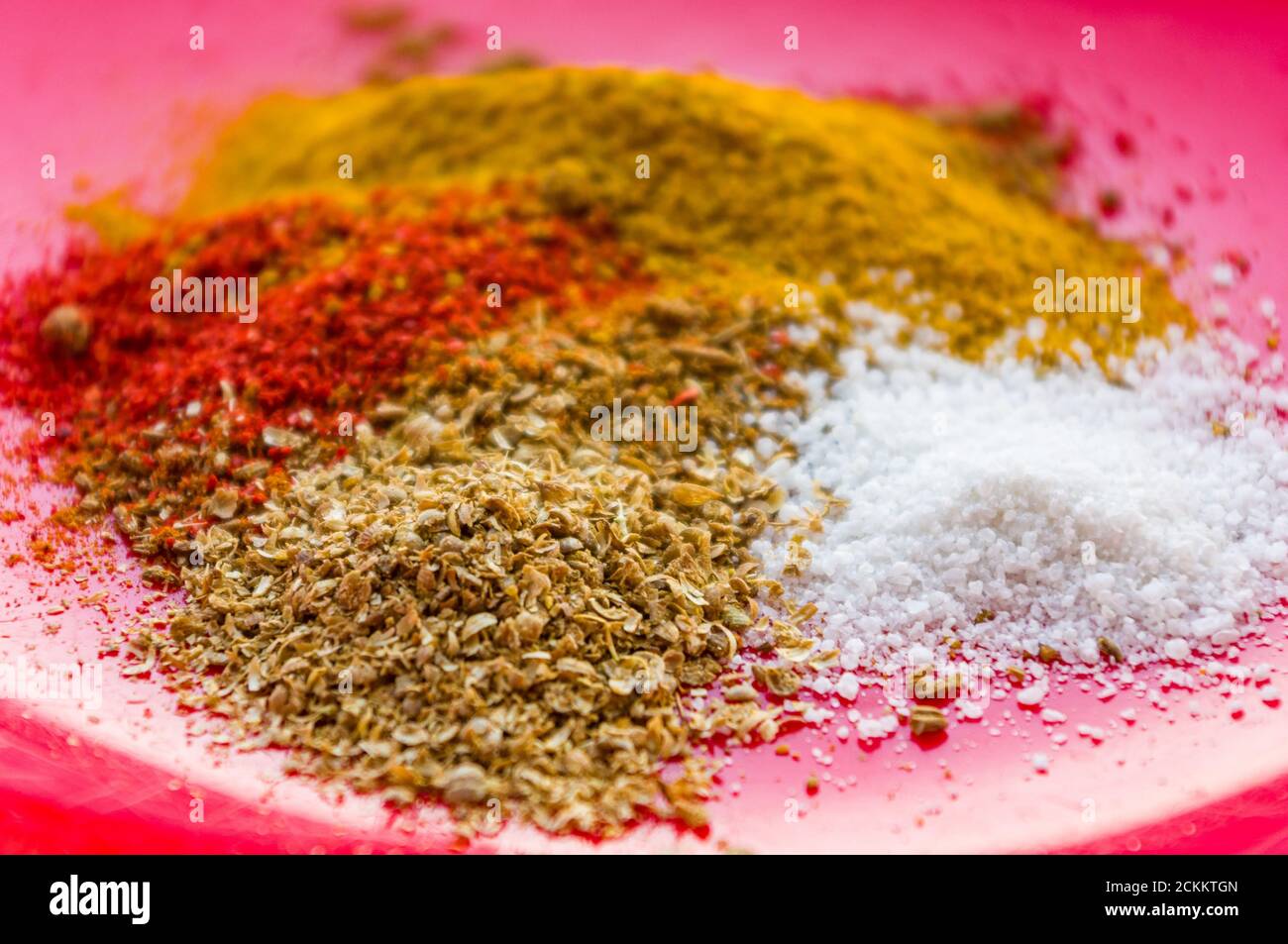Spices - red pepper, ground coriander, salt and turmeric on a red plate ...