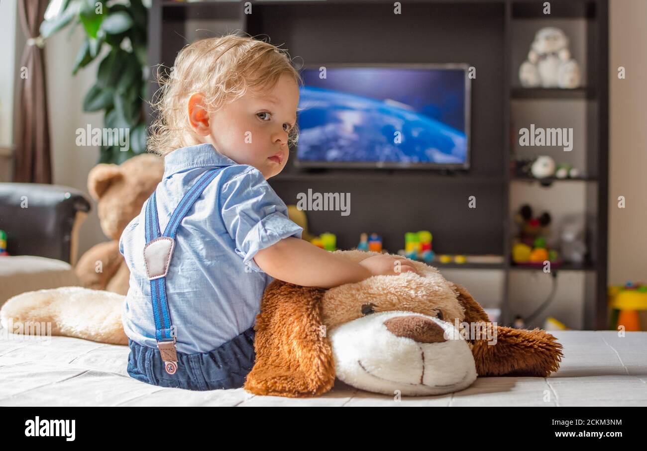 Cute baby boy and his dog plush toy watching TV sitting on a couch in ...