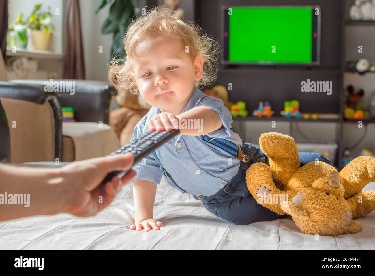 Cute baby boy taking the remote control to watch TV sitting on a couch ...