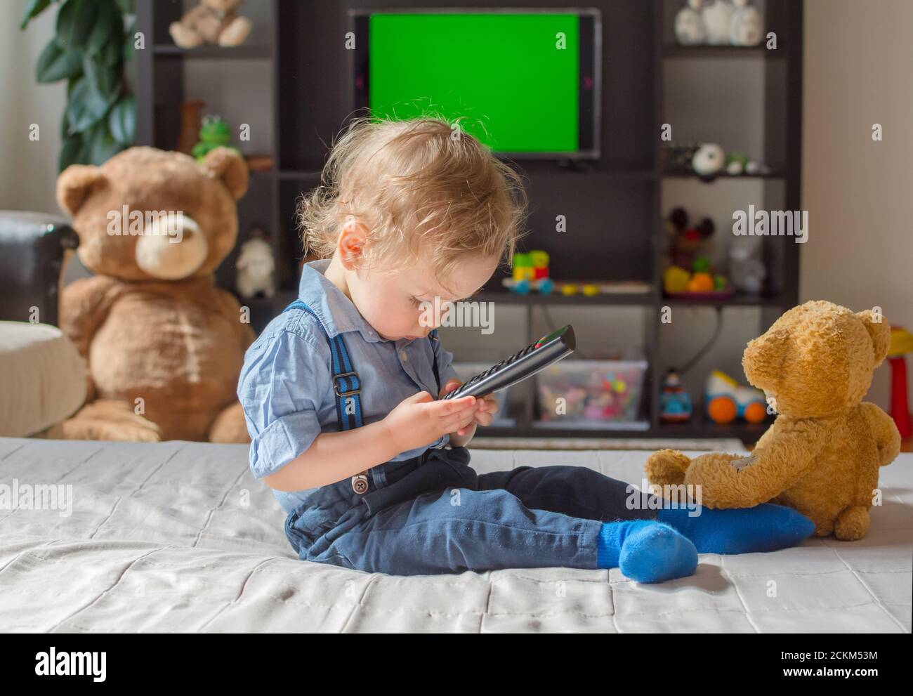 Cute baby boy playing with the remote control to watch TV sitting on a ...