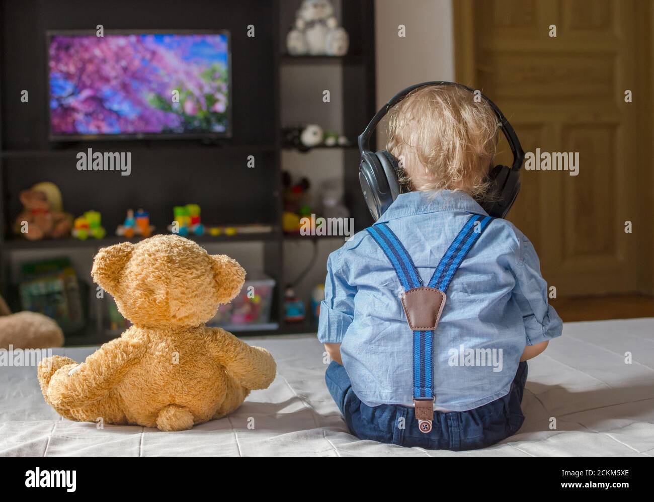 Cute baby boy with headphones and his teddy bear watching TV sitting on ...