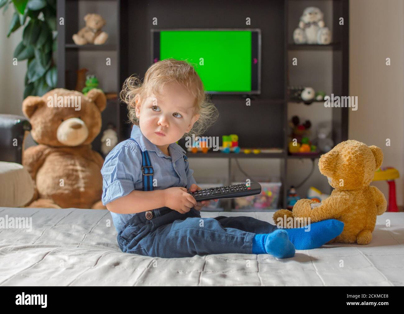 Cute baby boy playing with the remote control to watch TV sitting on a ...