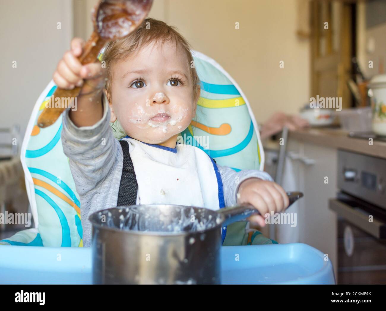 Funny baby child getting messy eating cereals or porridge by itself ...