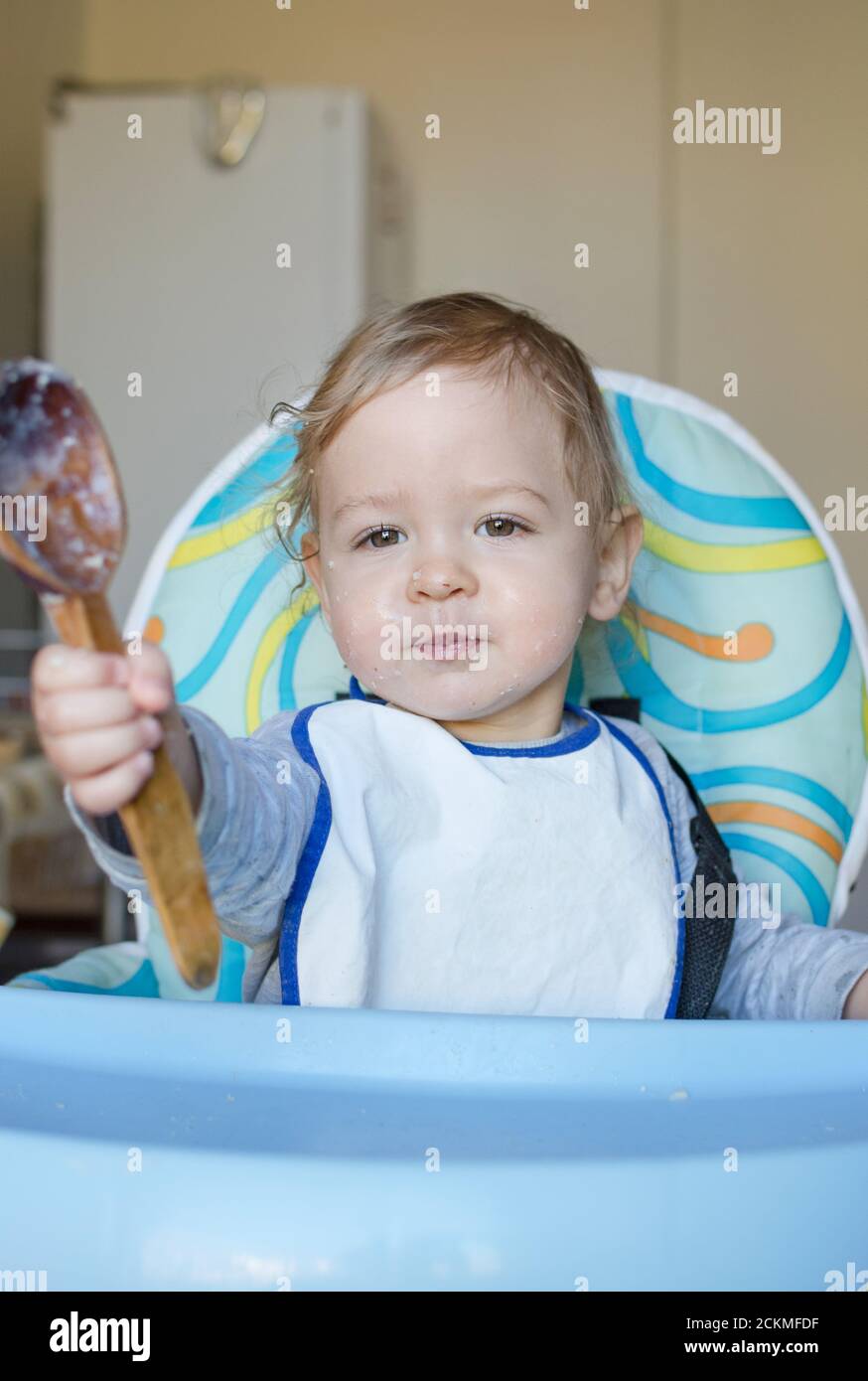 Cute baby child getting messy eating cereals or porridge by itself ...
