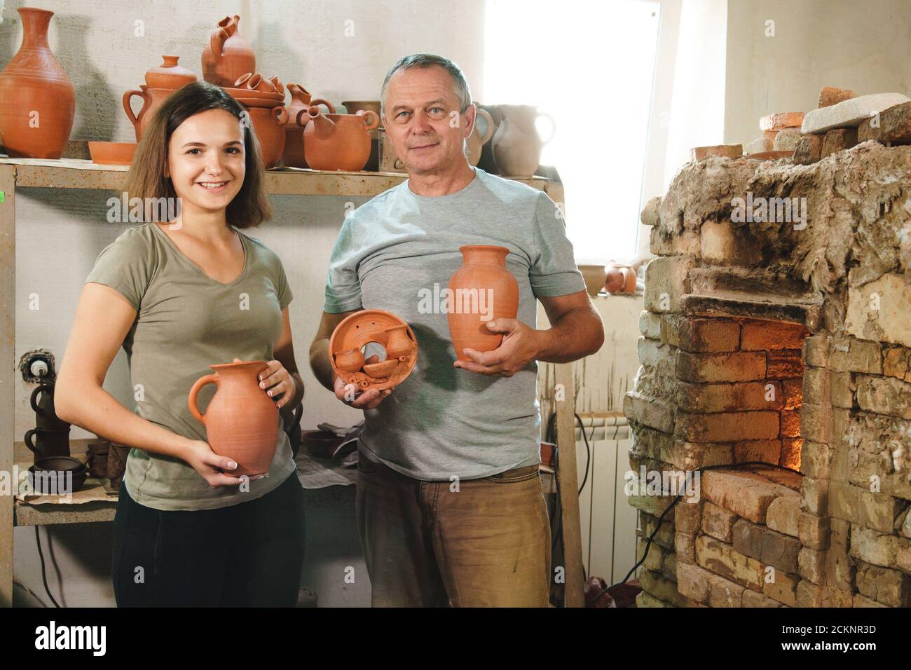 Father and daughter potters on brick pottery kiln background. Artisans ...