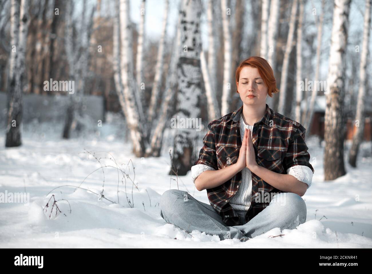 Girl praying to god in winter park. Woman sitting on snow in forest and ...