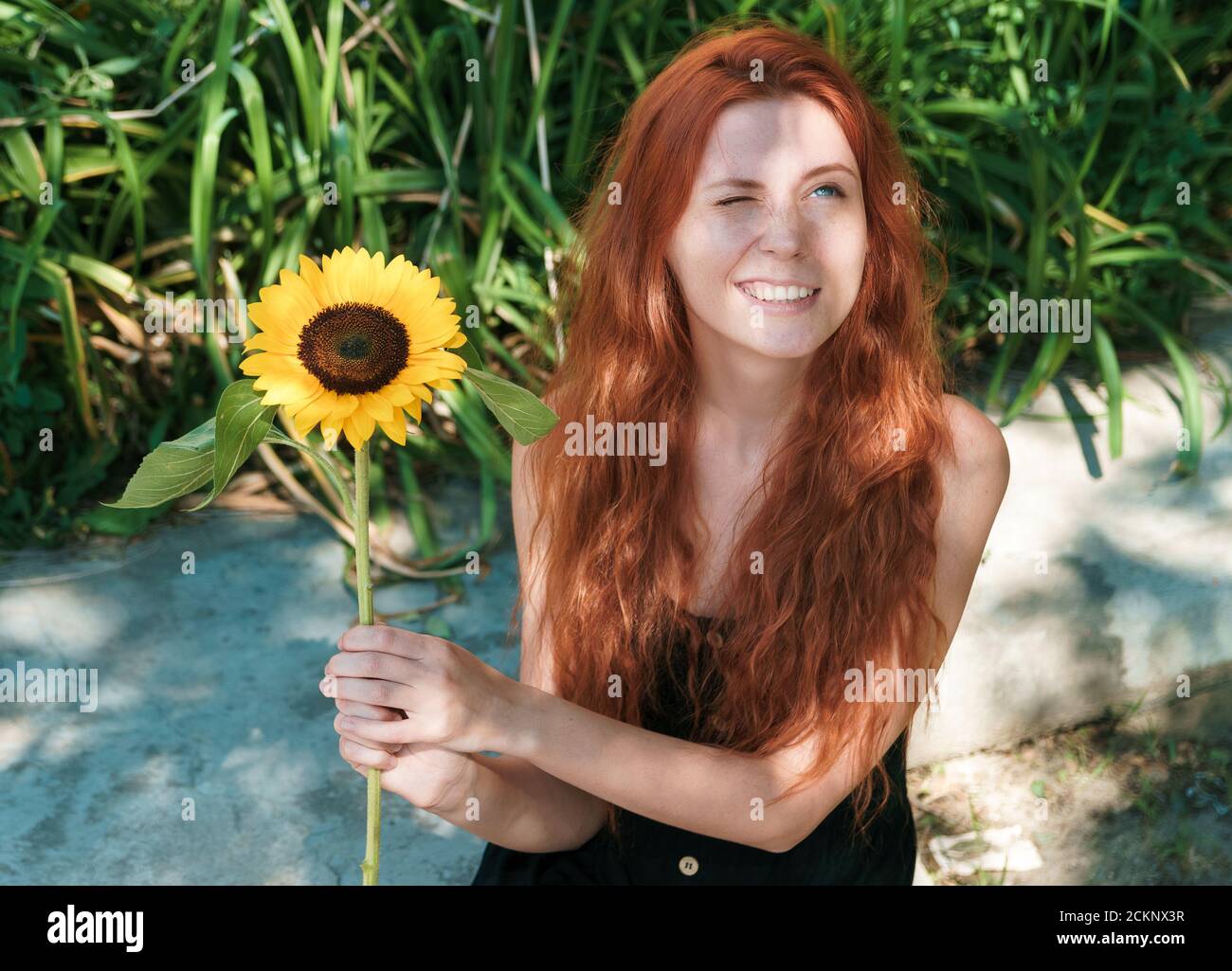 Ginger girl with sunflower in shade of tree looks at sun. Summer mood ...