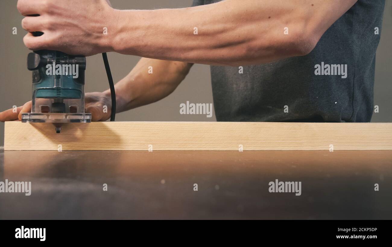 Carpenter chamfers edge from wooden board. Milling cutter and sawdust ...