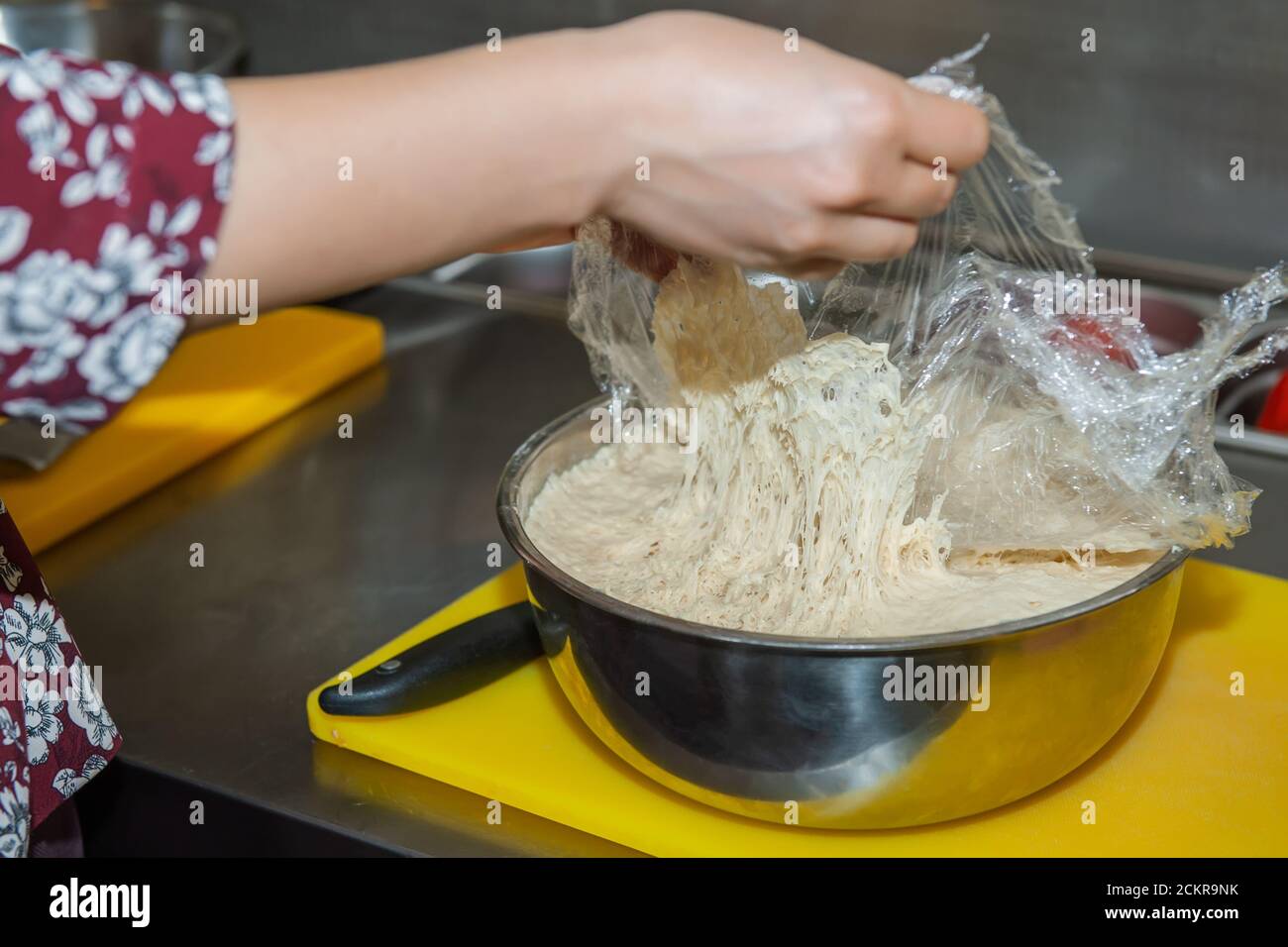 Pulling the plastic wrap off the raised bread dough in a metal mixing ...