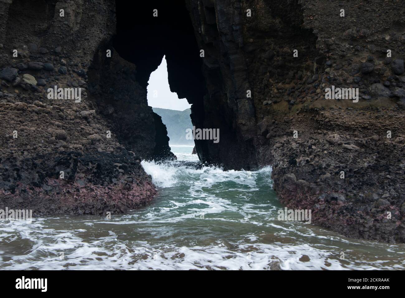 The keyhole rock on Piha beach with waves crashing through the cave ...