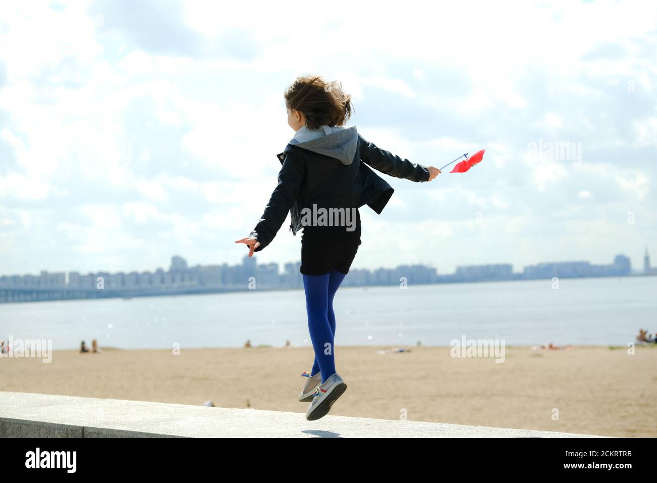 Happy girl with red wind spinner walking on the embankment on blue sky ...