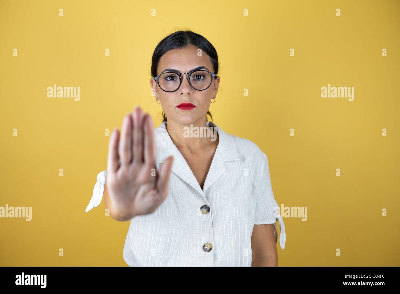 Beautiful woman over yellow background serious and doing stop sing with ...