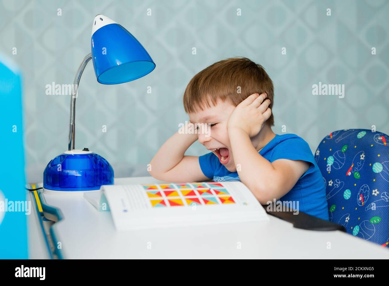 A schoolboy boy sits at a desk and holds his head and screams Stock ...