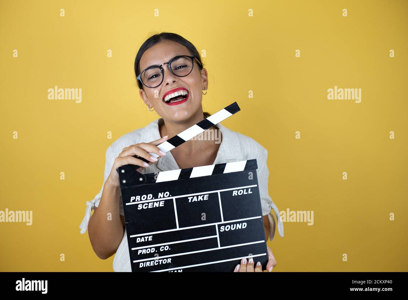 Beautiful woman over yellow background holding clapperboard very happy ...