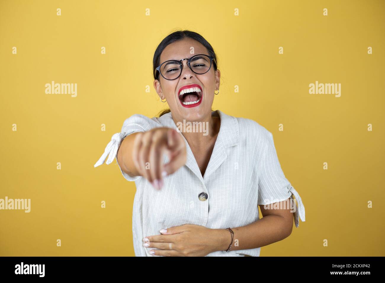 Beautiful woman over yellow background laughing at you, pointing finger ...