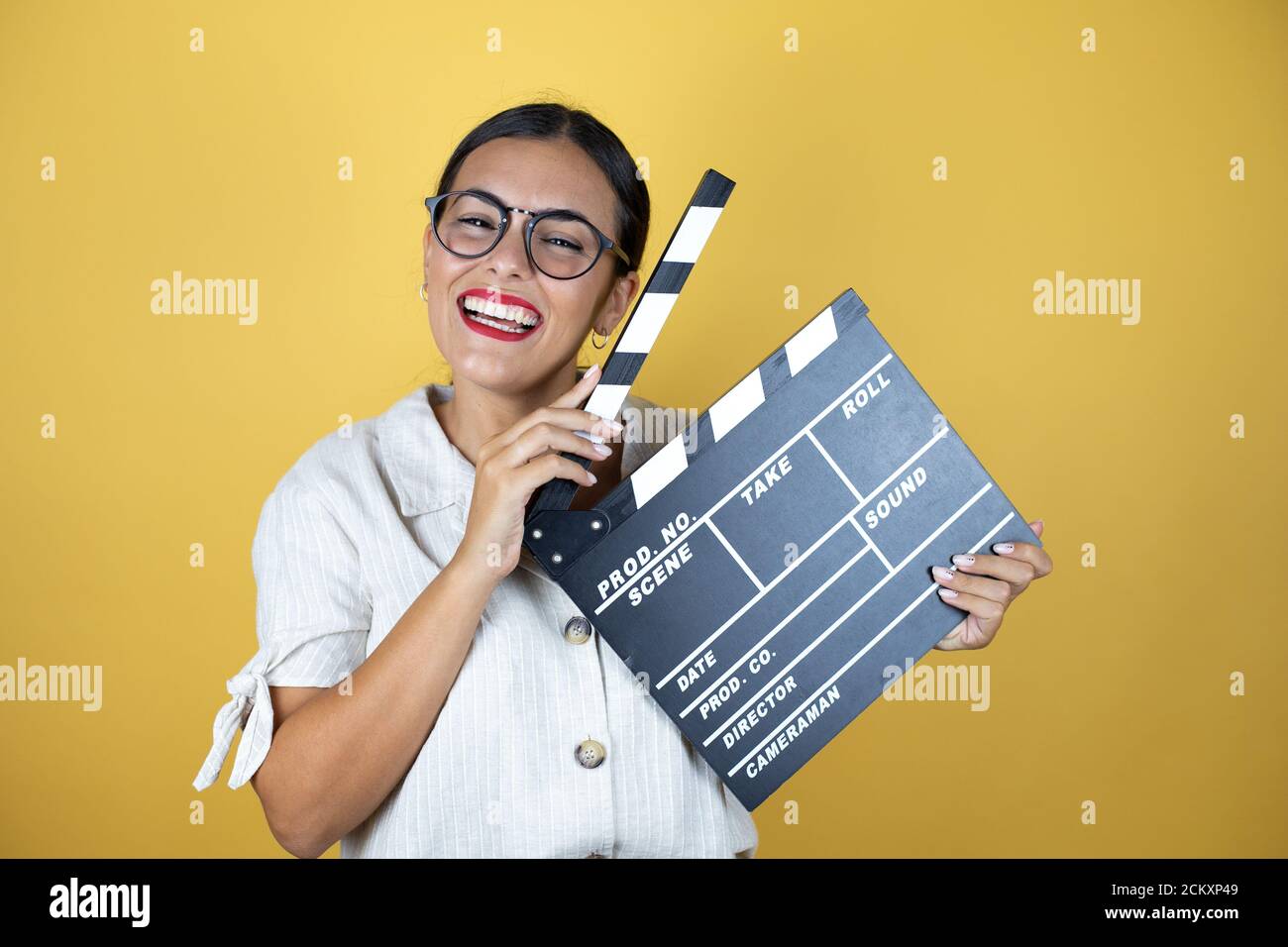 Beautiful woman over yellow background holding clapperboard very happy ...
