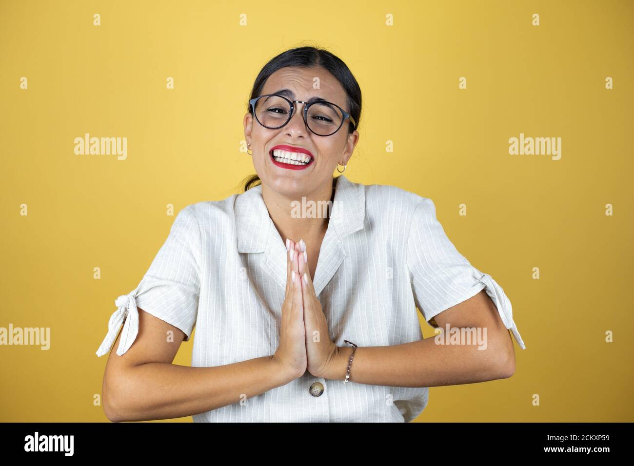 Beautiful woman over yellow background begging and praying with hands ...