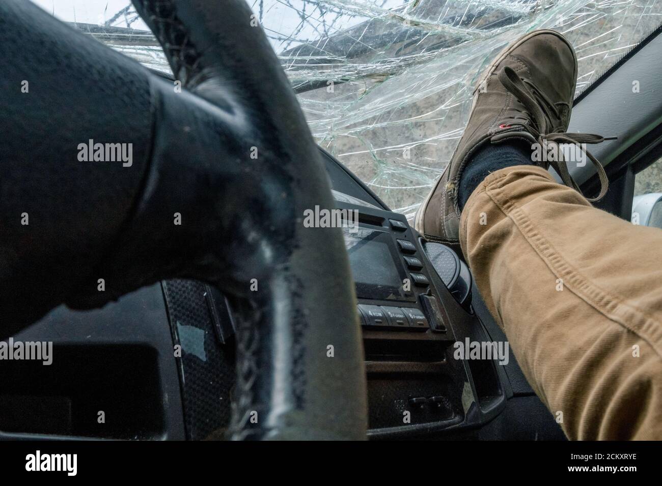 Foot on the dashboard on the background of the broken windshield of the ...