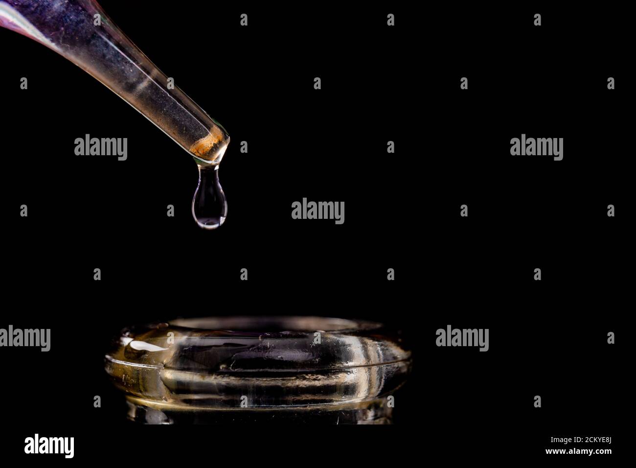 A drop of blue liquid dripping from the pipette. Glass accessories in ...