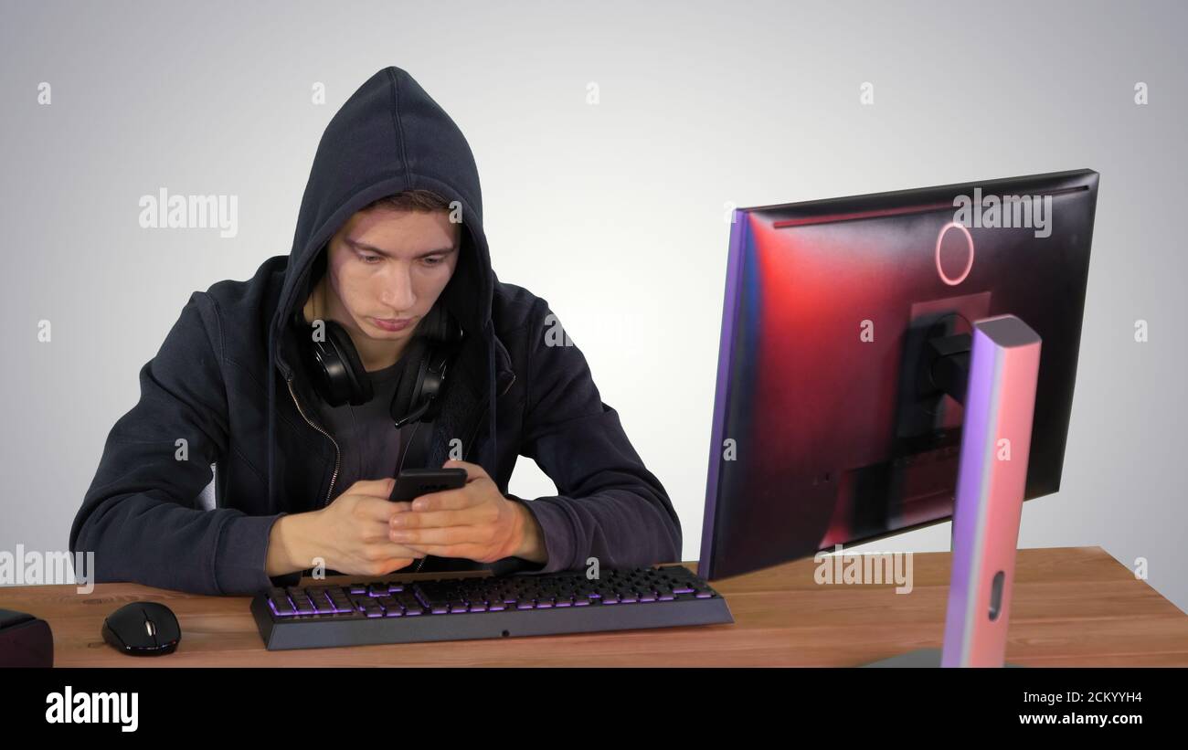 Hooded hacker using laptop and smartphone on gradient background Stock ...