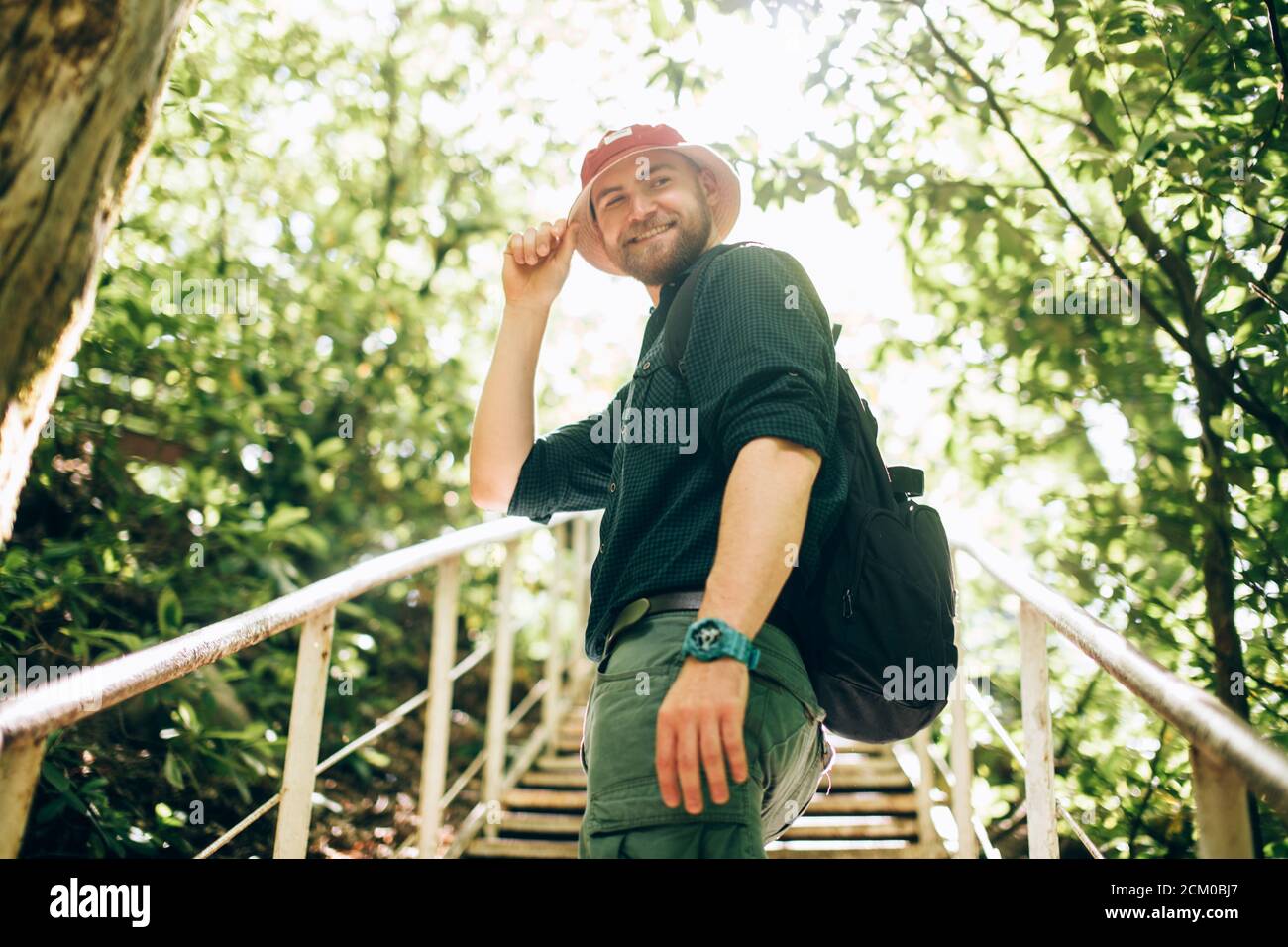 Smiling traveler in red hat, wearing backpack climbing up on wooden ...