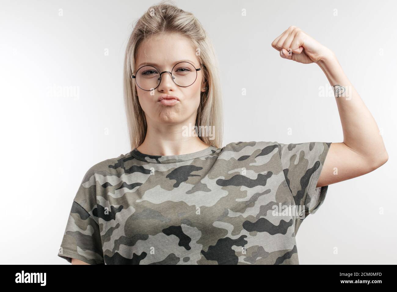 Cheerful smiling young woman in dazzle paint t-shirt flexing biceps ...
