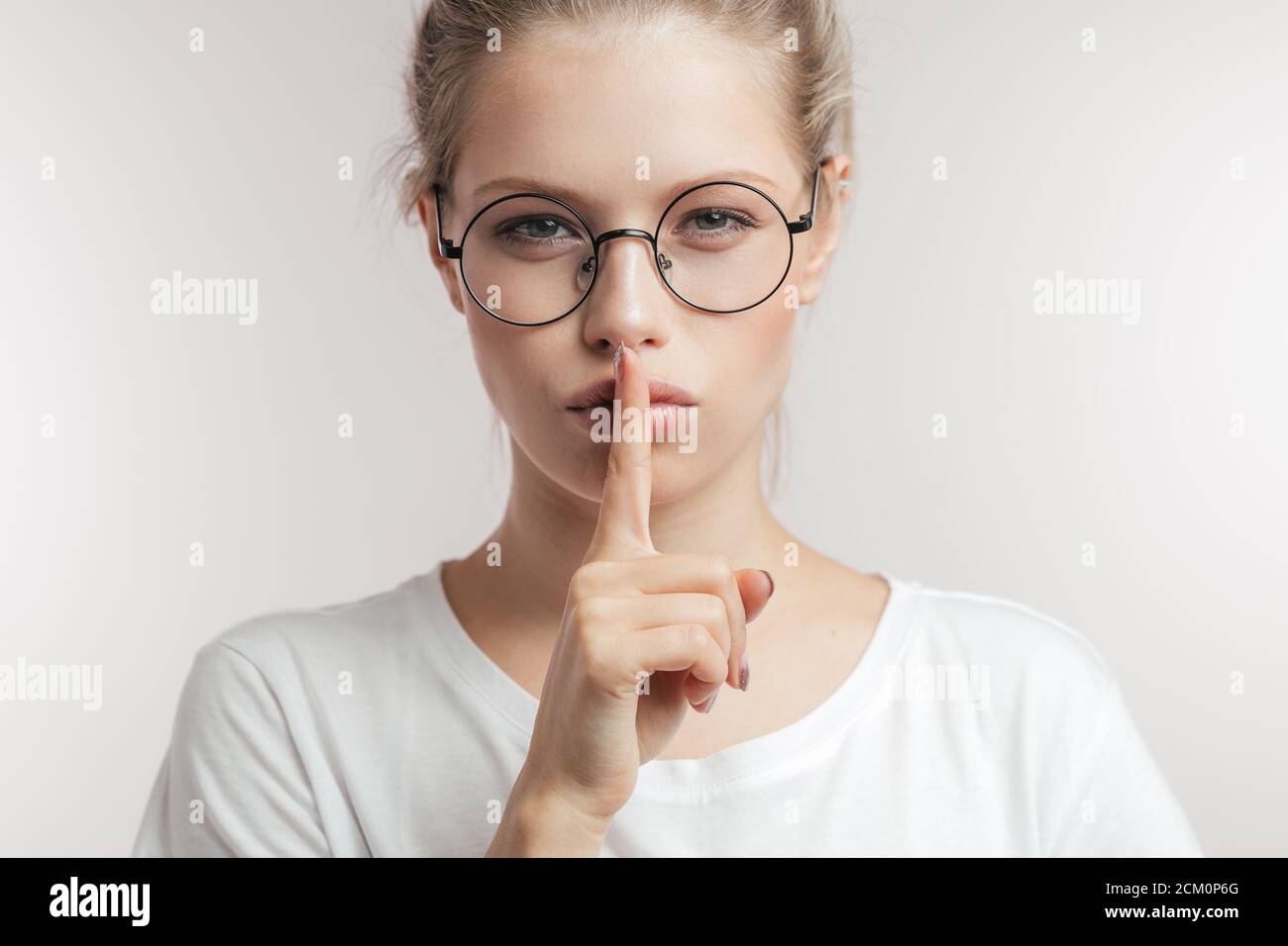 Finger on lips - silent gesture. Caucasian young woman in round ...