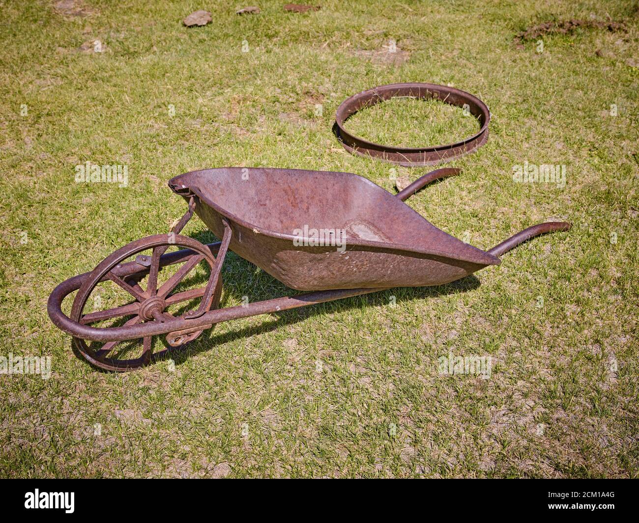 An old timey rusted metal wheel barrow sits in the grass in the sun ...