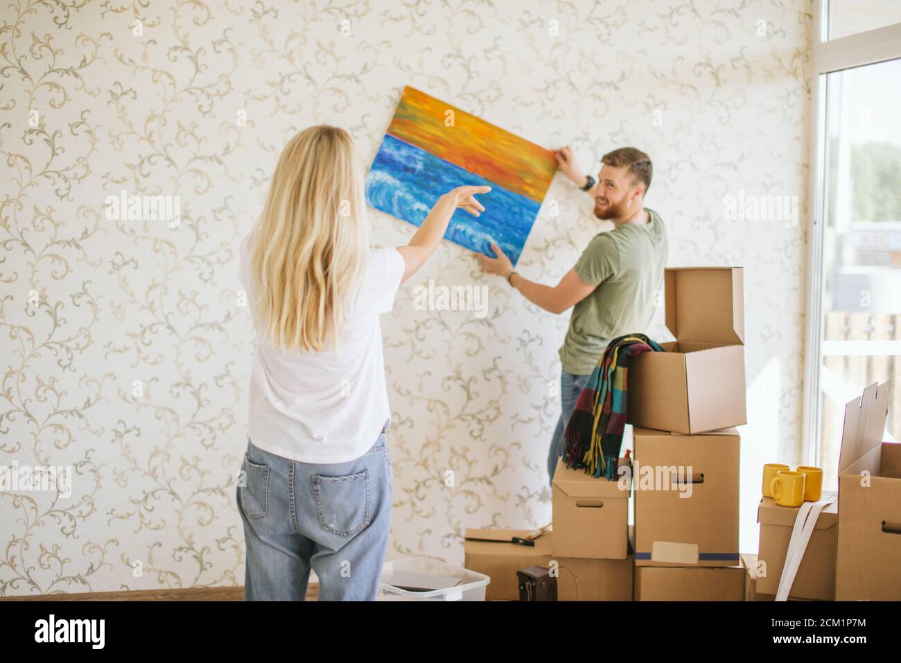 Moving house. Young Couple hanging picture on wall in new home Stock ...