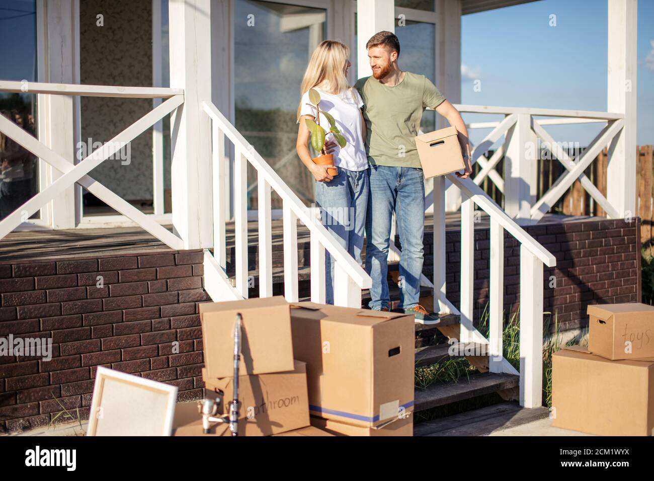 Husband and wife standing in front of new buying home with boxes ...