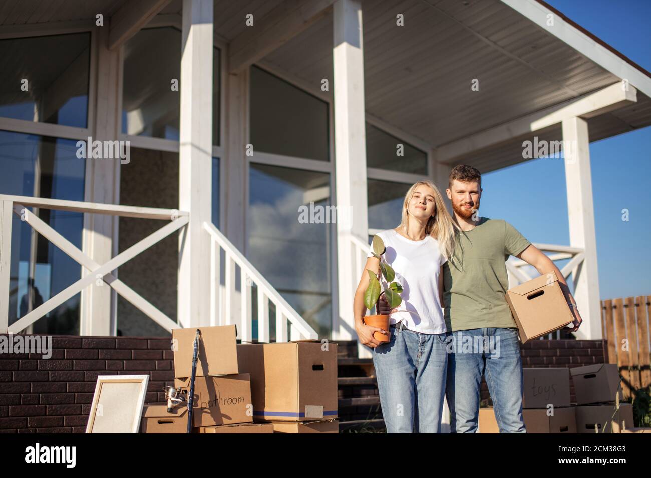 Husband and wife standing in front of new buying home with boxes ...