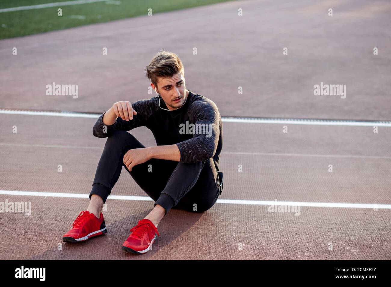 Runner wearing black clothes and red shoes resting on race track in ...