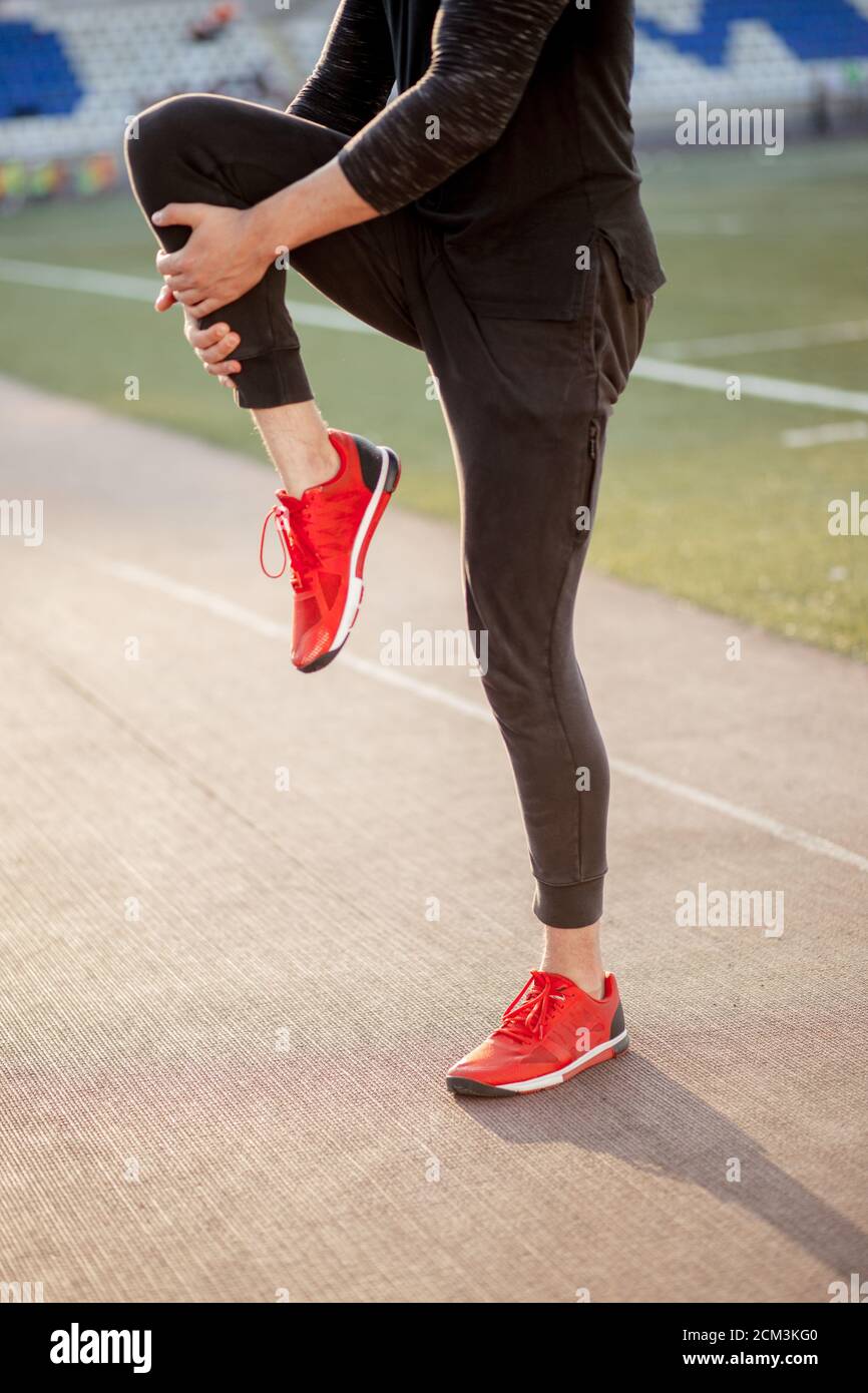 Man runner stretching legs preparing for run training on stadium tracks ...