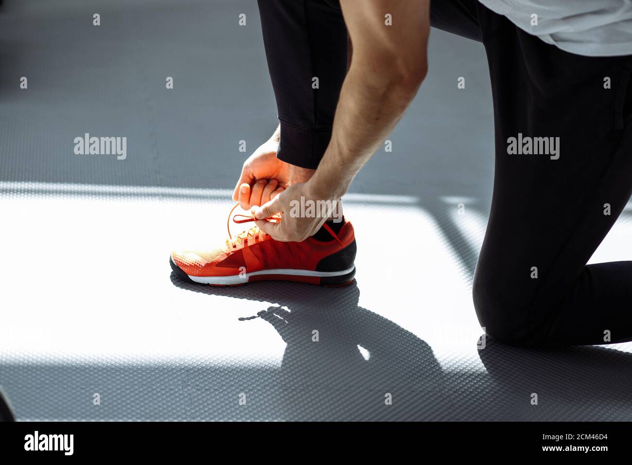 Handsome caucasian sportsman lacing red sport shoes in gym with water ...