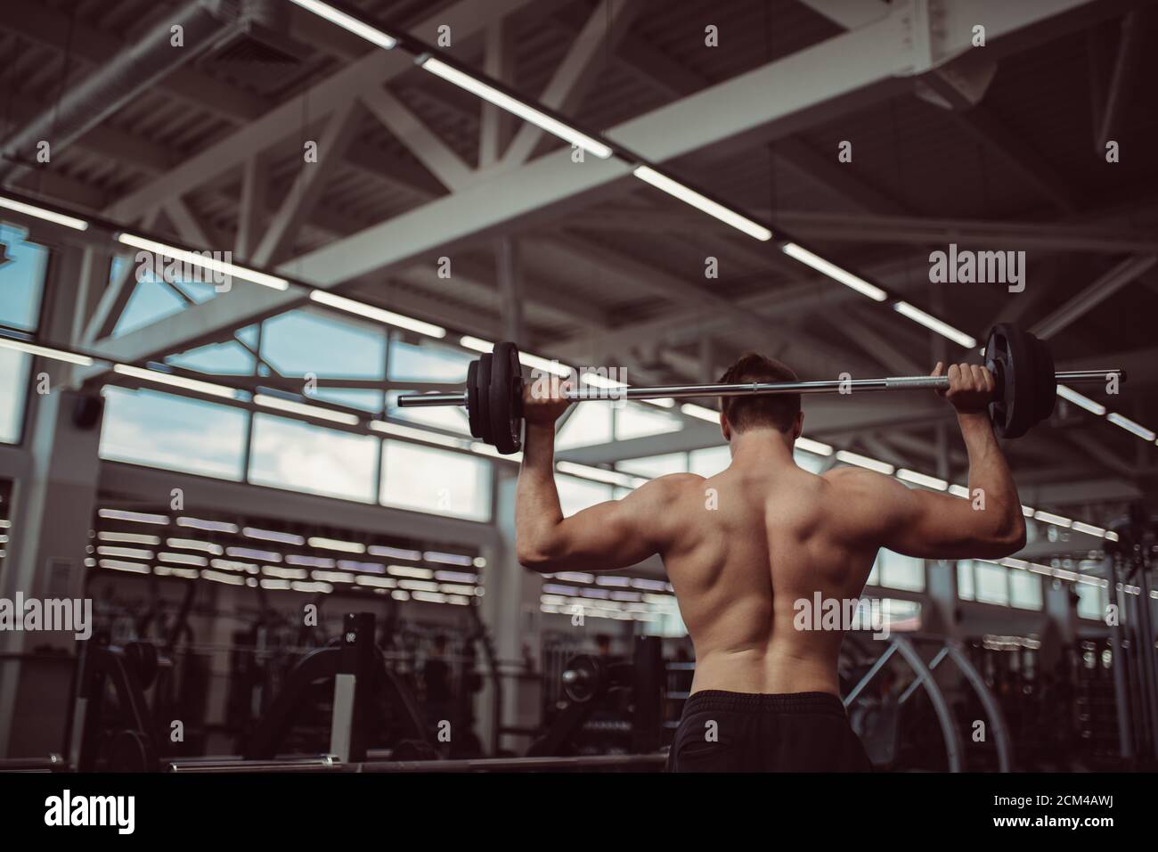 Power Man lifting barbell in a gym with training machines, rear view of ...