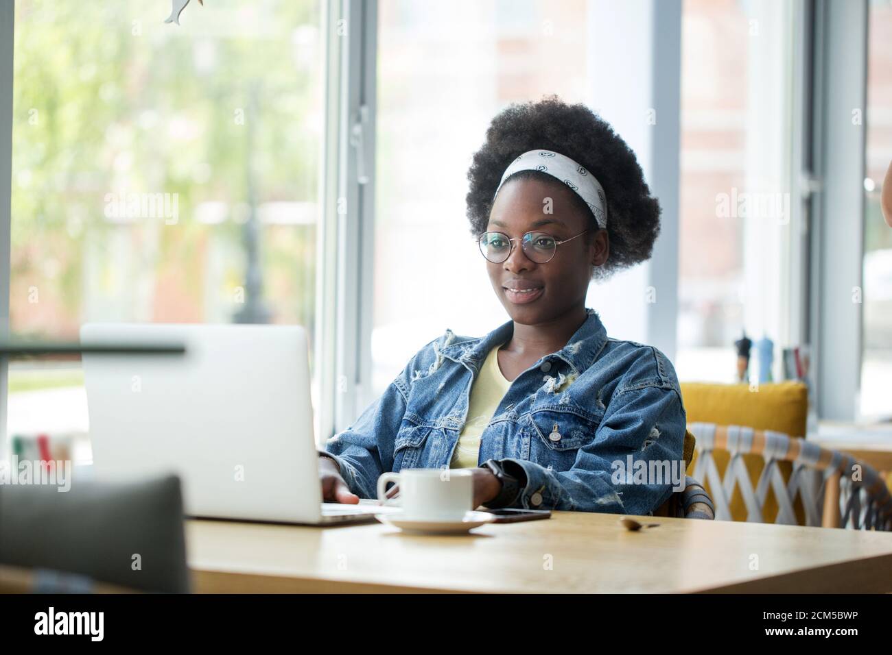 Intelligent African female student dressed casually, working at laptop ...