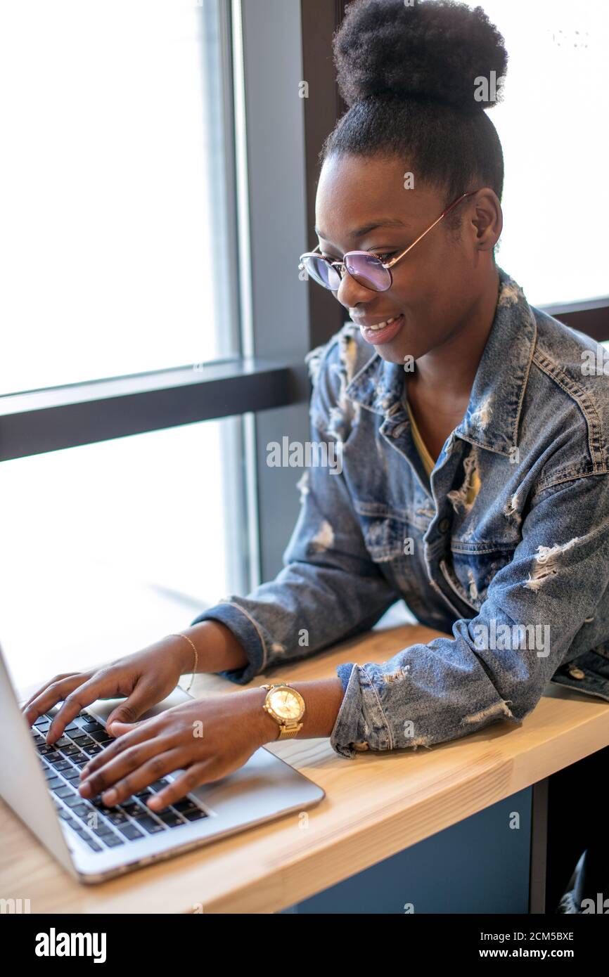 Intelligent African female student dressed casually, working at laptop ...