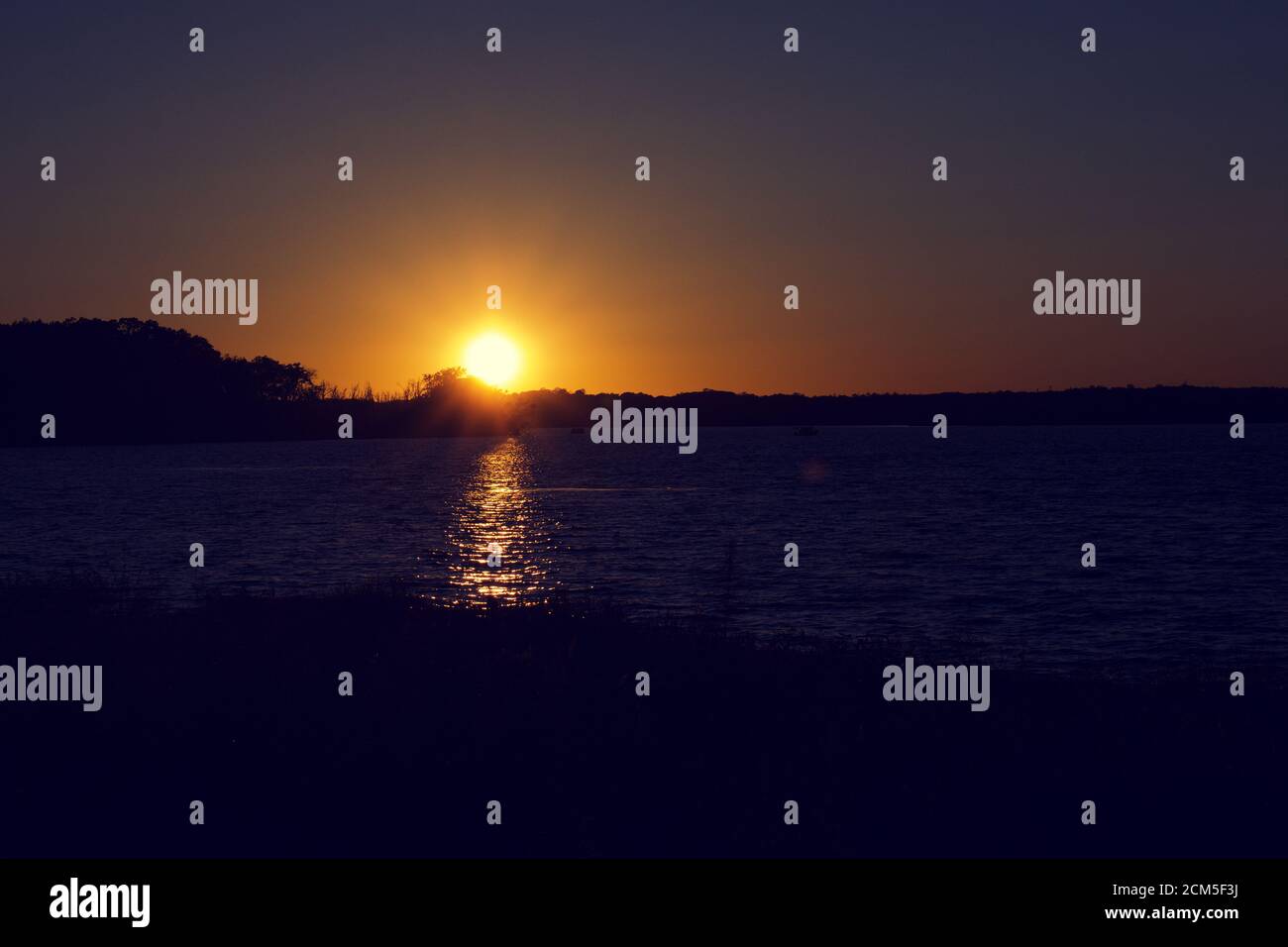 Sun setting over Belmont Bay with silhouette of trees and cliff Stock ...