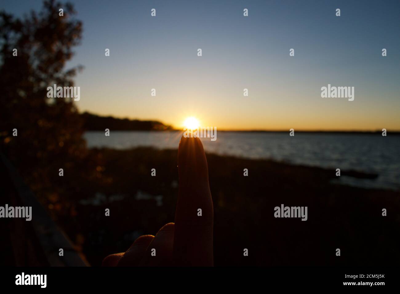 Sun setting over Belmont Bay with silhouette of trees and cliff Stock ...